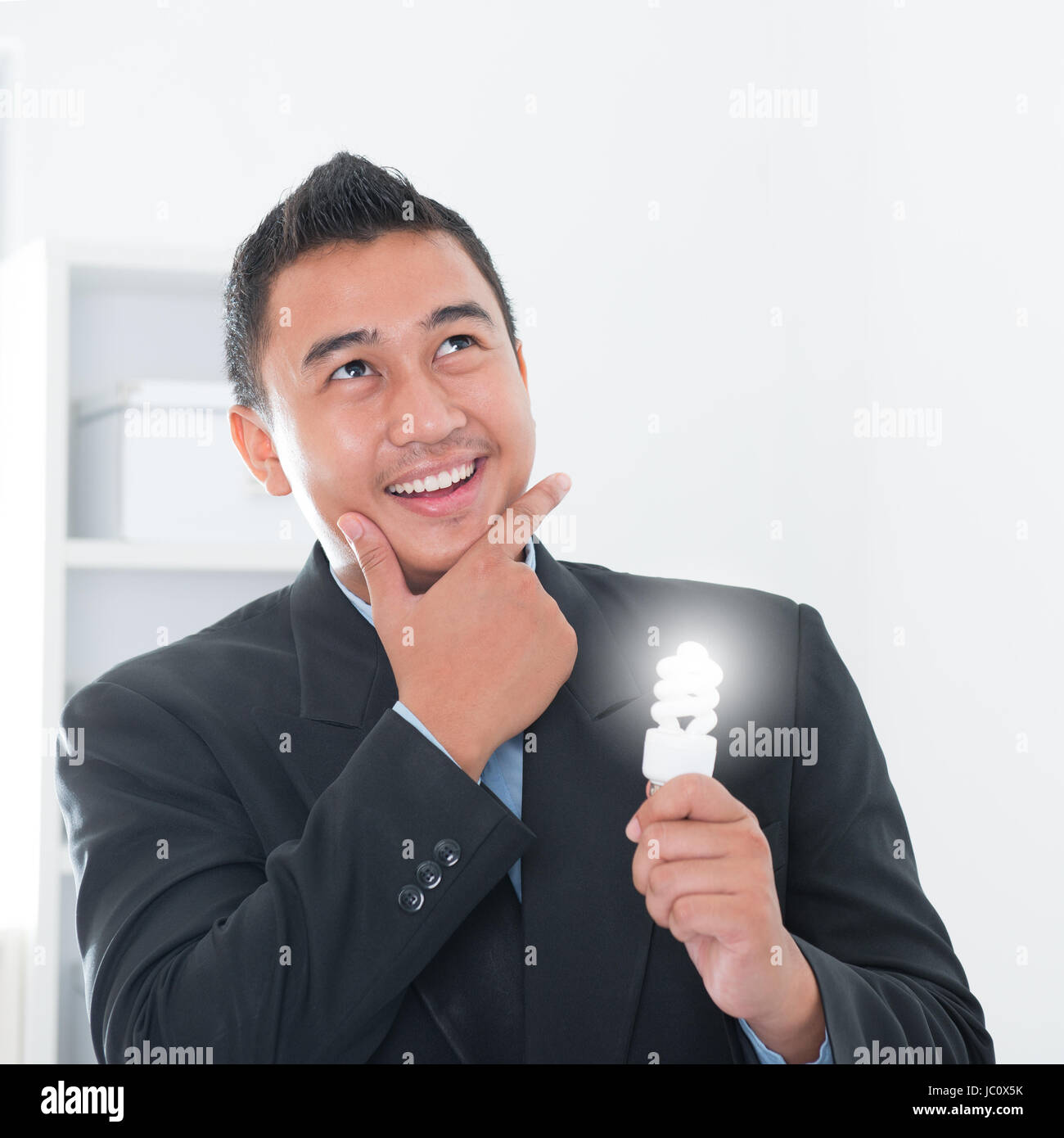 Southeast Asian businessman holding an illuminated light bulb, thinking ...