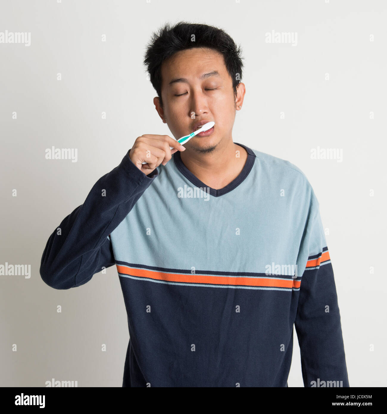 Sleepy Southeast Asian male brushing teeth while eyes closing in a ...
