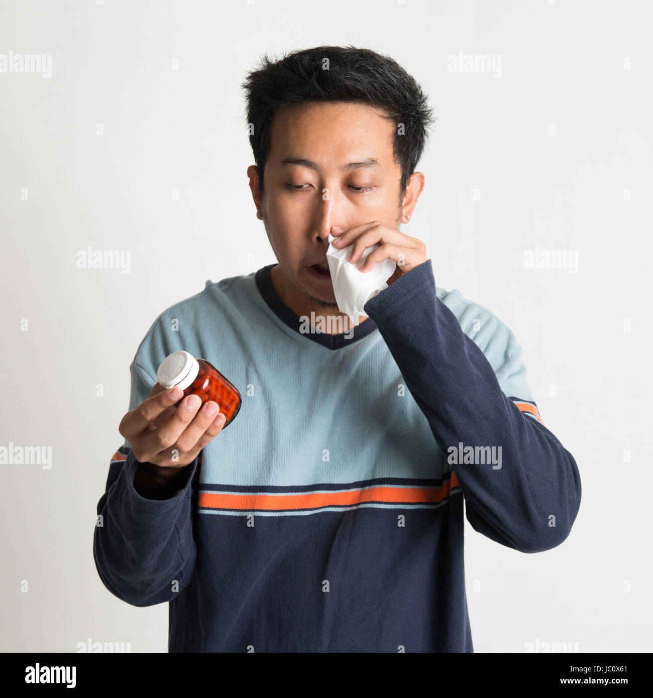 Asian male sneezing and holding medicine bottle, on plain background ...