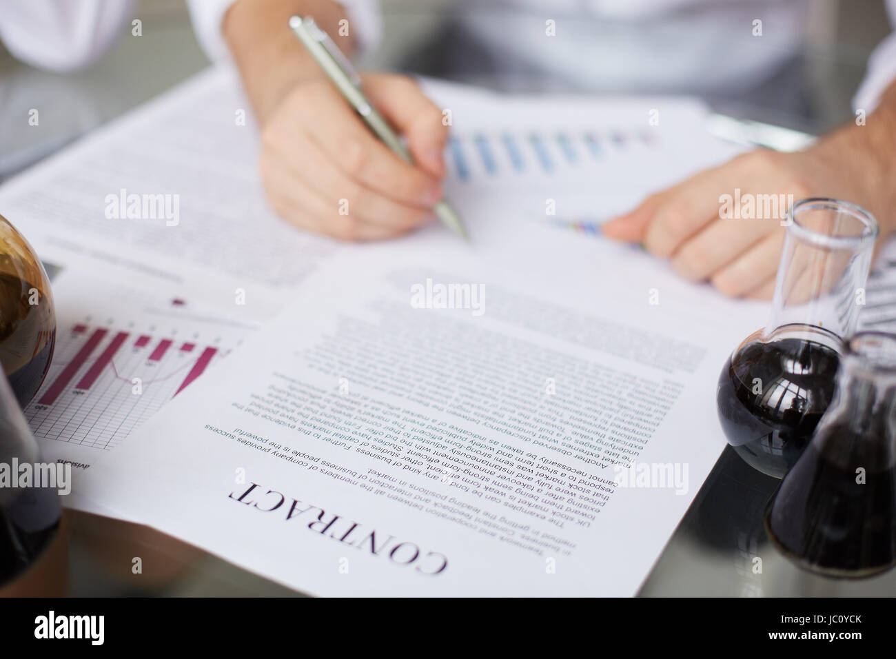 Test-tubes with liquid oil and paper agreement being signed by human ...