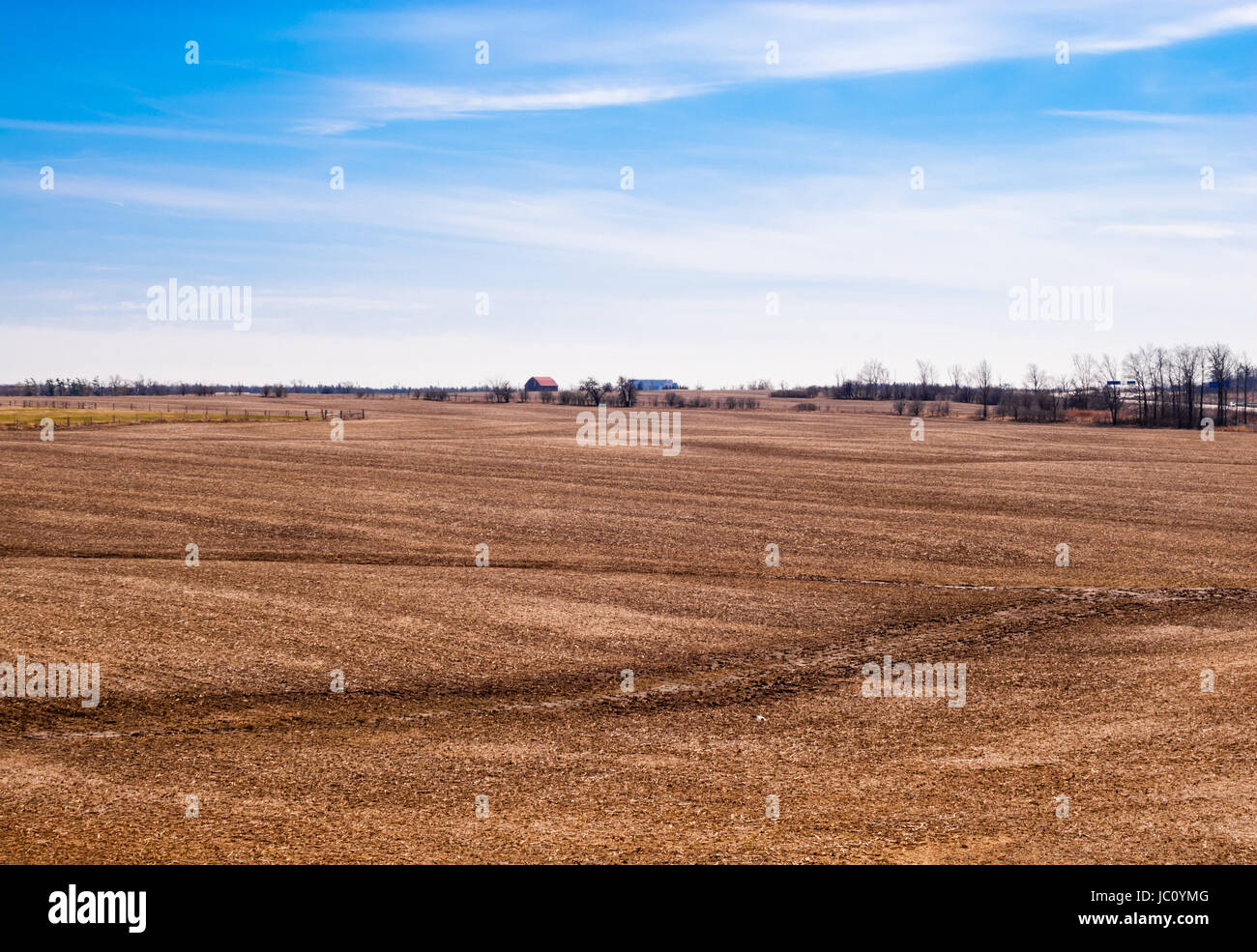 Empty brown farm fields with barn in distance against partly cloudy sky ...