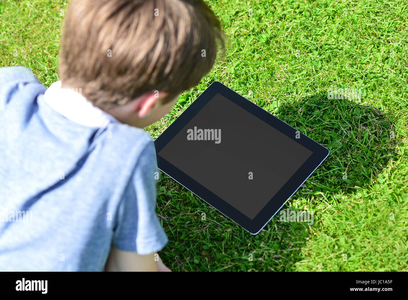 Boy lying on the grass, looking at tablet screen Stock Photo - Alamy
