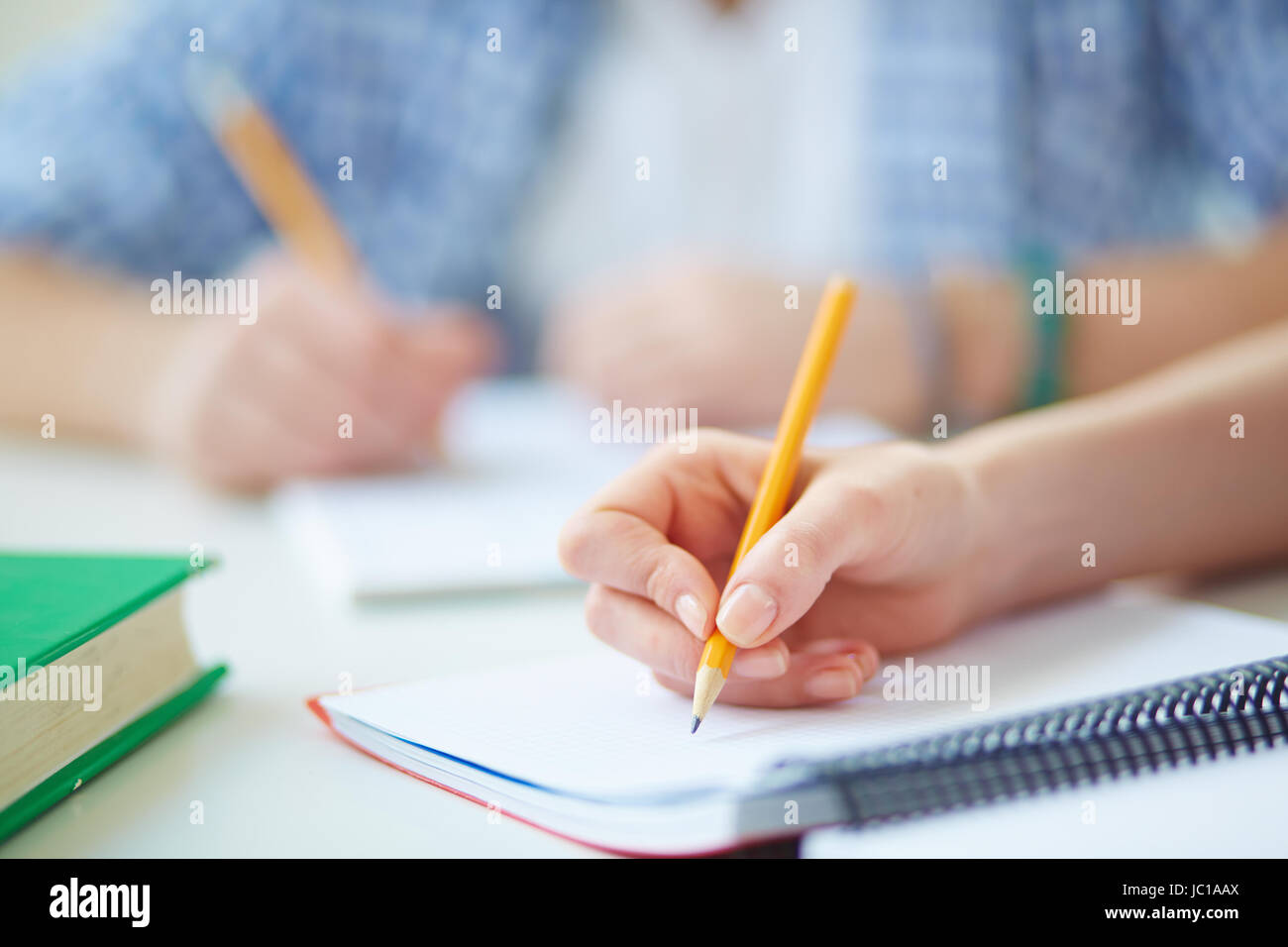 Hand of student with pencil carrying out written task or writing ...
