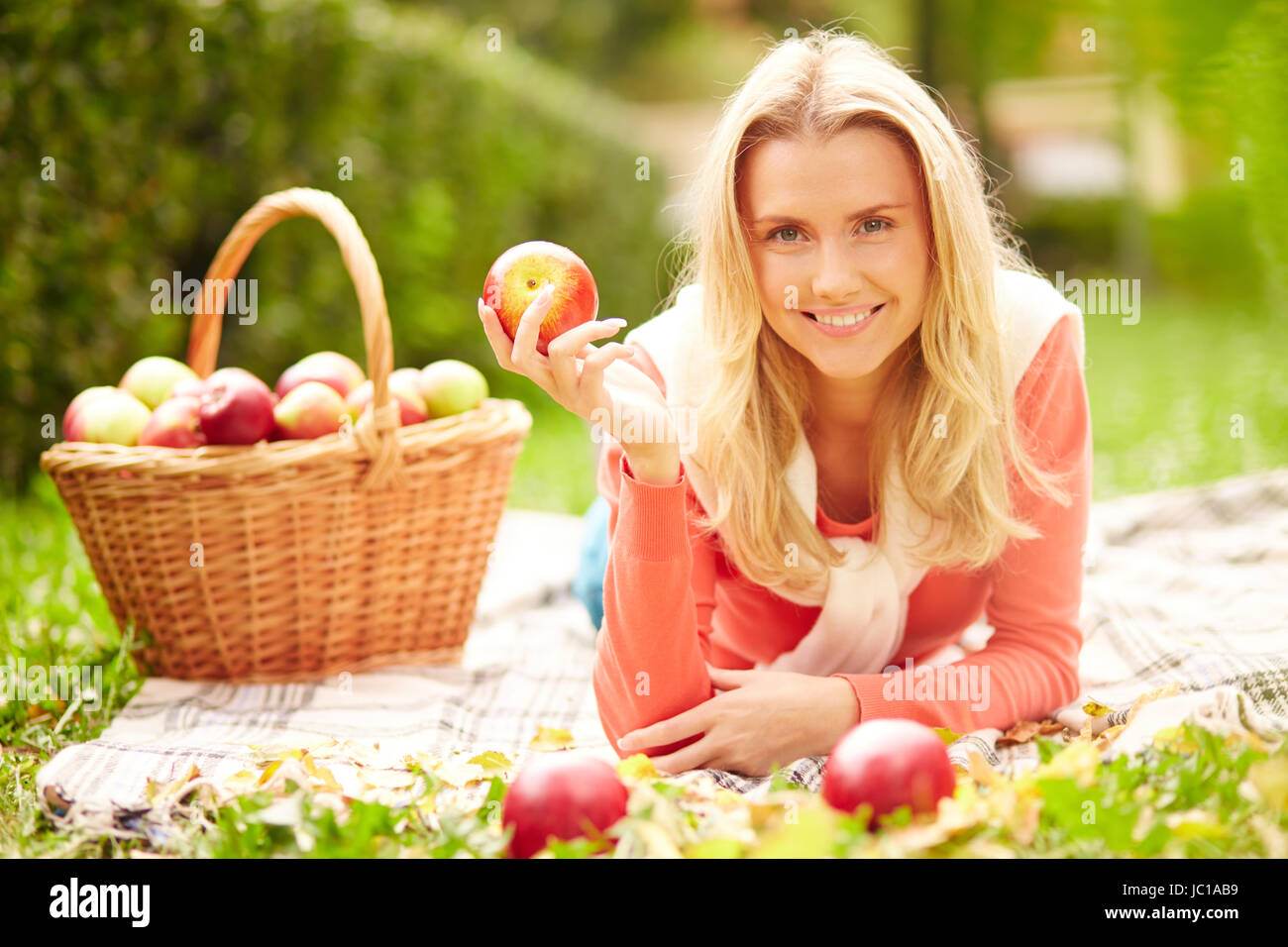 Happy girl with ripe red apple looking at camera while lying on grass ...