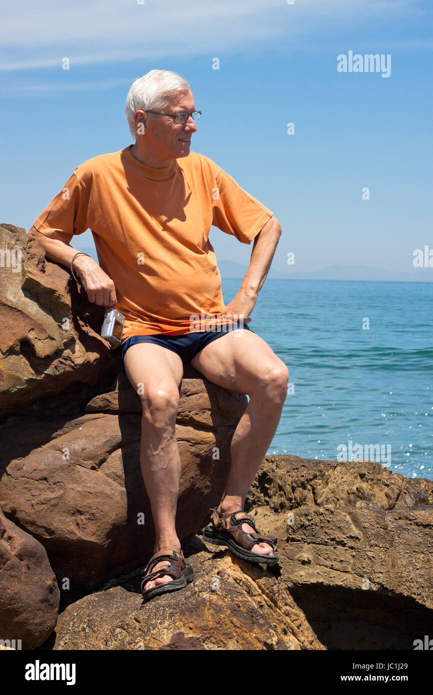 Portrait of senior tourist man sitting on the rocky beach Stock Photo ...