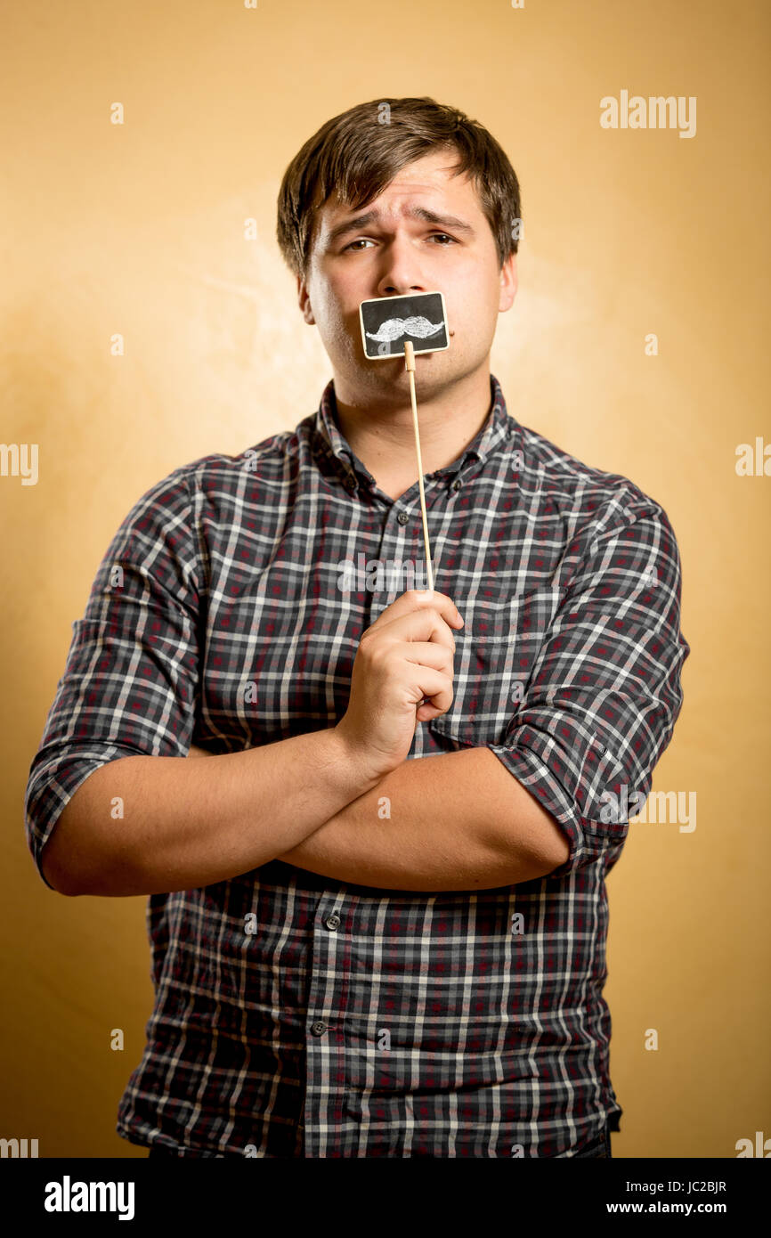 Portrait of thoughtful hipster guy posing with fake mustache on stick ...