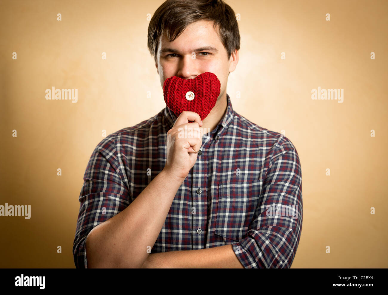 Handsome smiling man holding red heart at mouth Stock Photo - Alamy