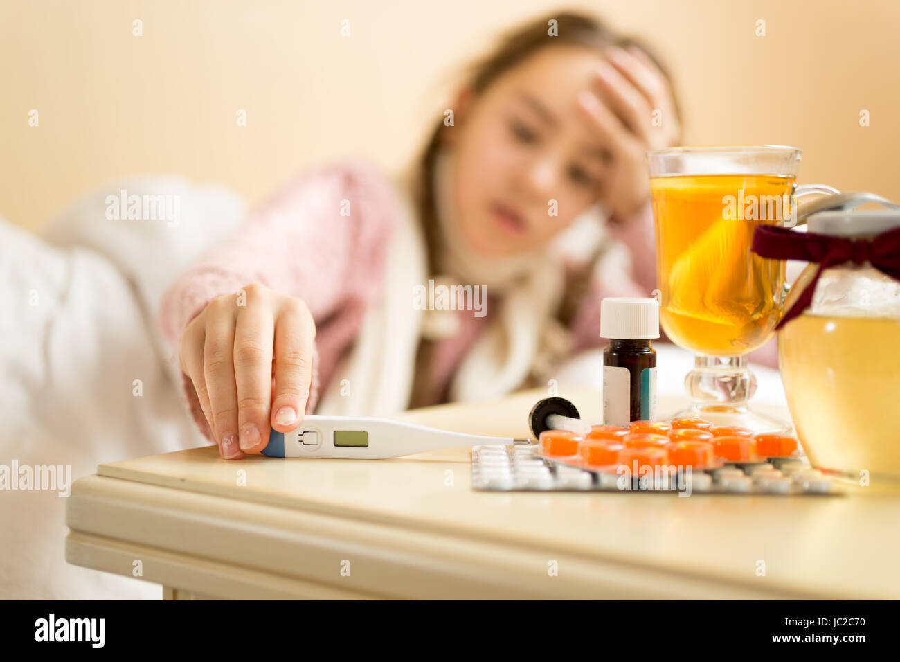 Out of focus portrait of sick girl lying in bed and taking thermometer ...