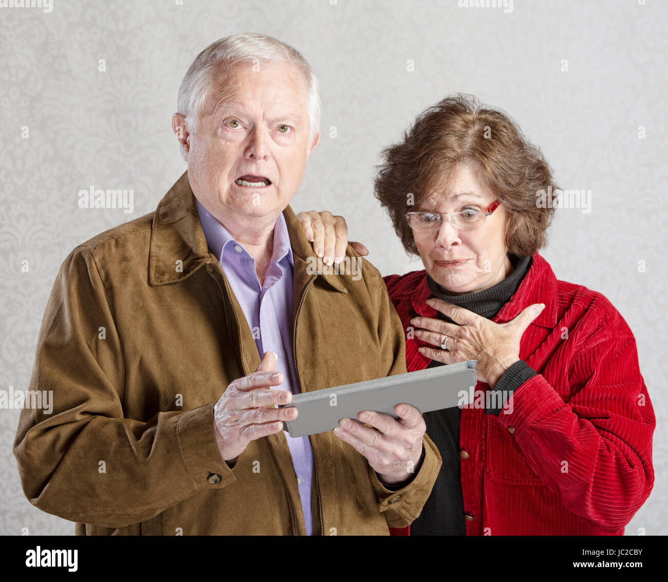 Startled man and woman looking at computer tablet Stock Photo - Alamy