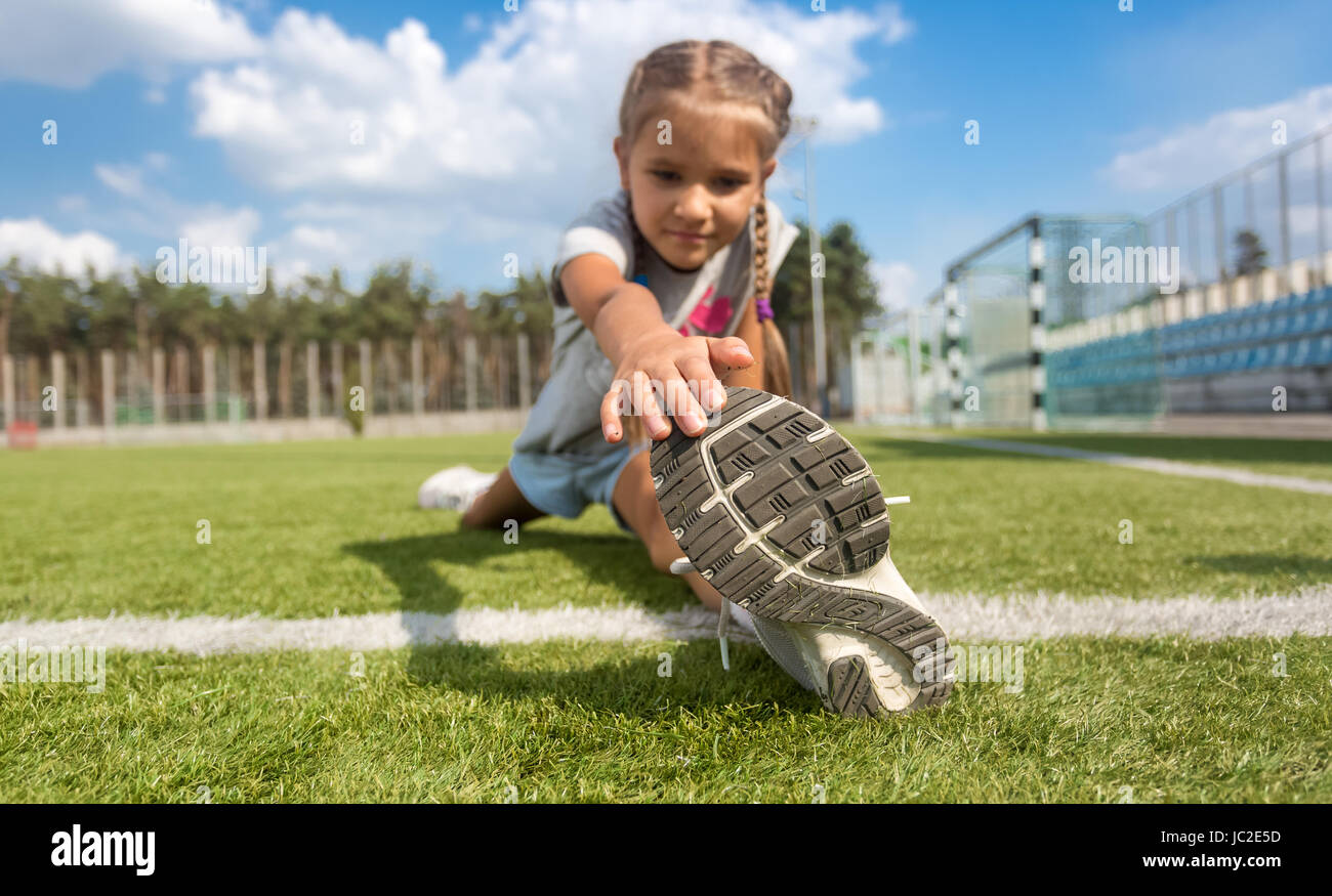 Closeup shot of young girl stretching legs on soccer field at sunny day ...