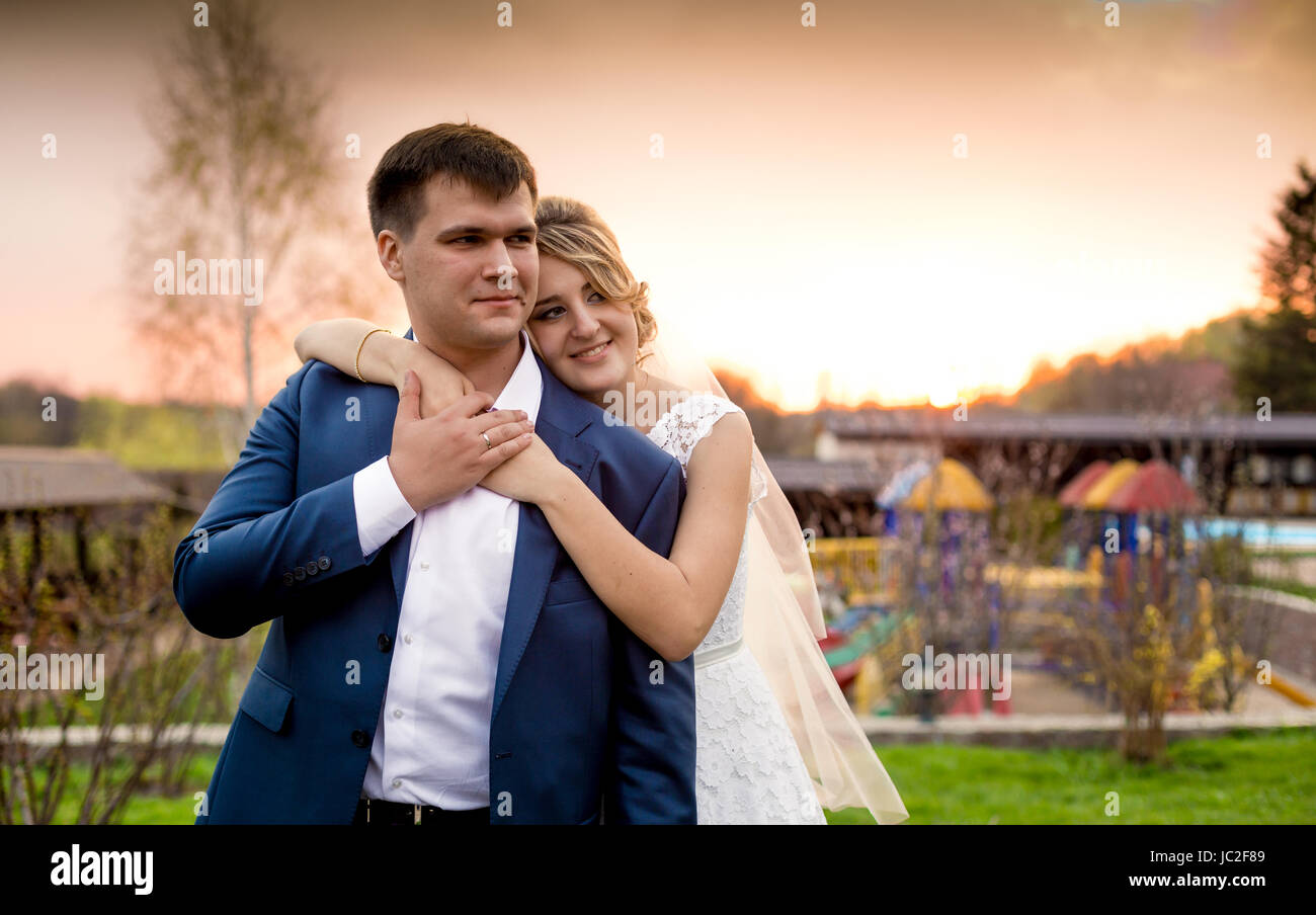 Portrait of happy bride hugging groom from back at beautiful sunset ...