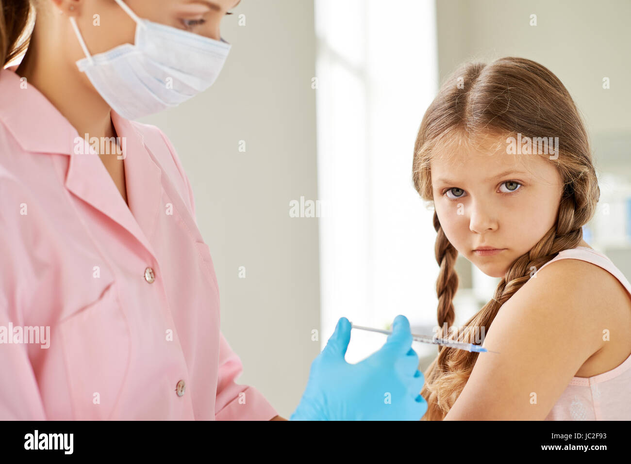 Sulky girl looking at camera while doctor making her an injection in ...