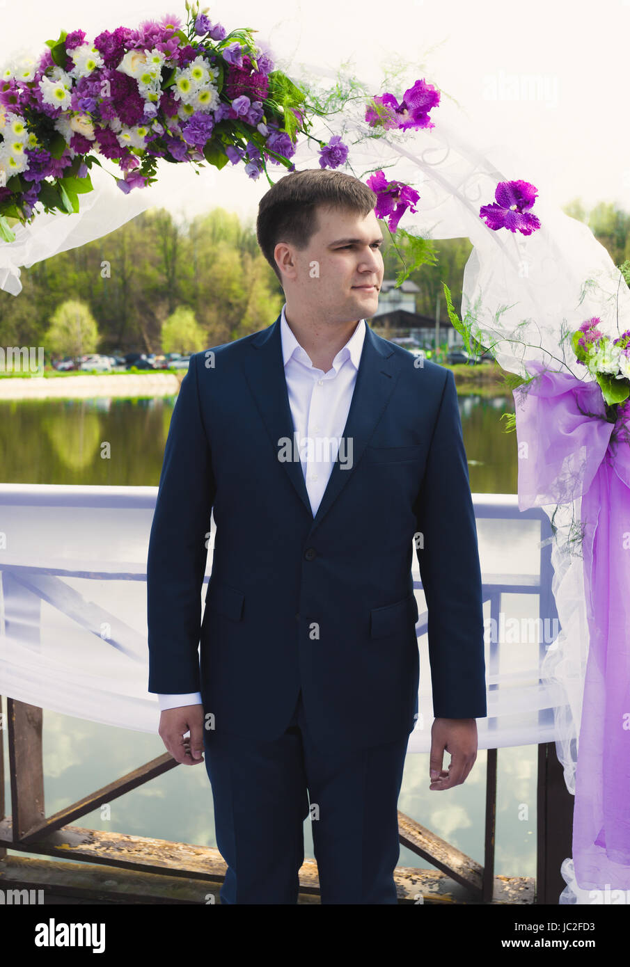 Young handsome groom waiting for bride under floral arch at ceremony ...