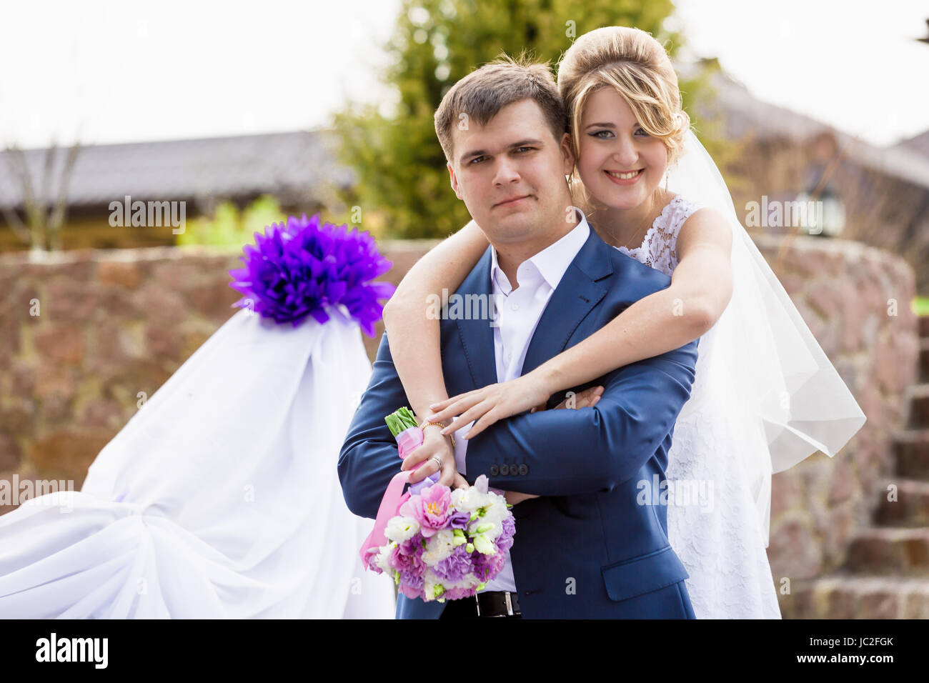 Portrait of beautiful bride hugging groom by the shoulders at park ...