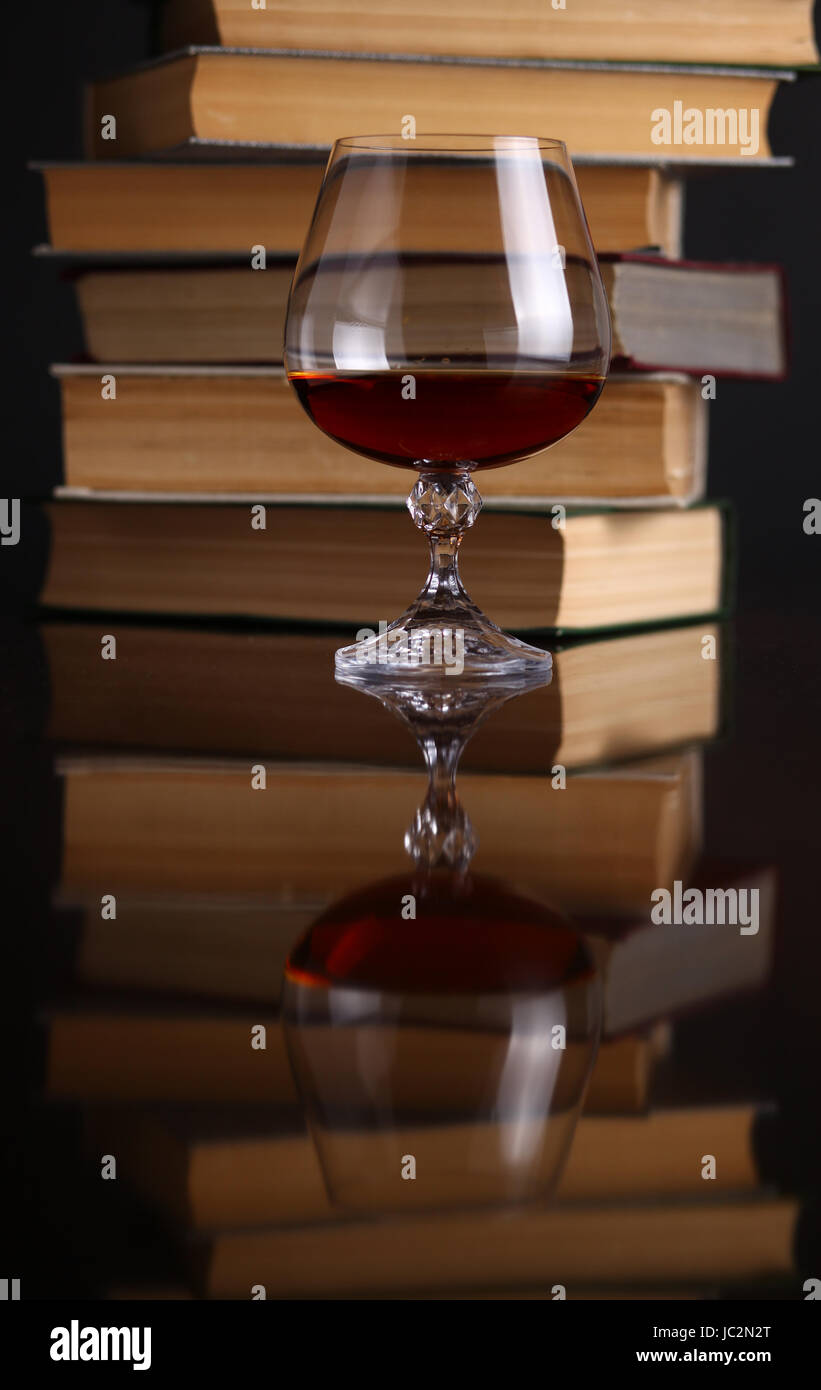Glass of brandy on a reflective surface with books Stock Photo - Alamy