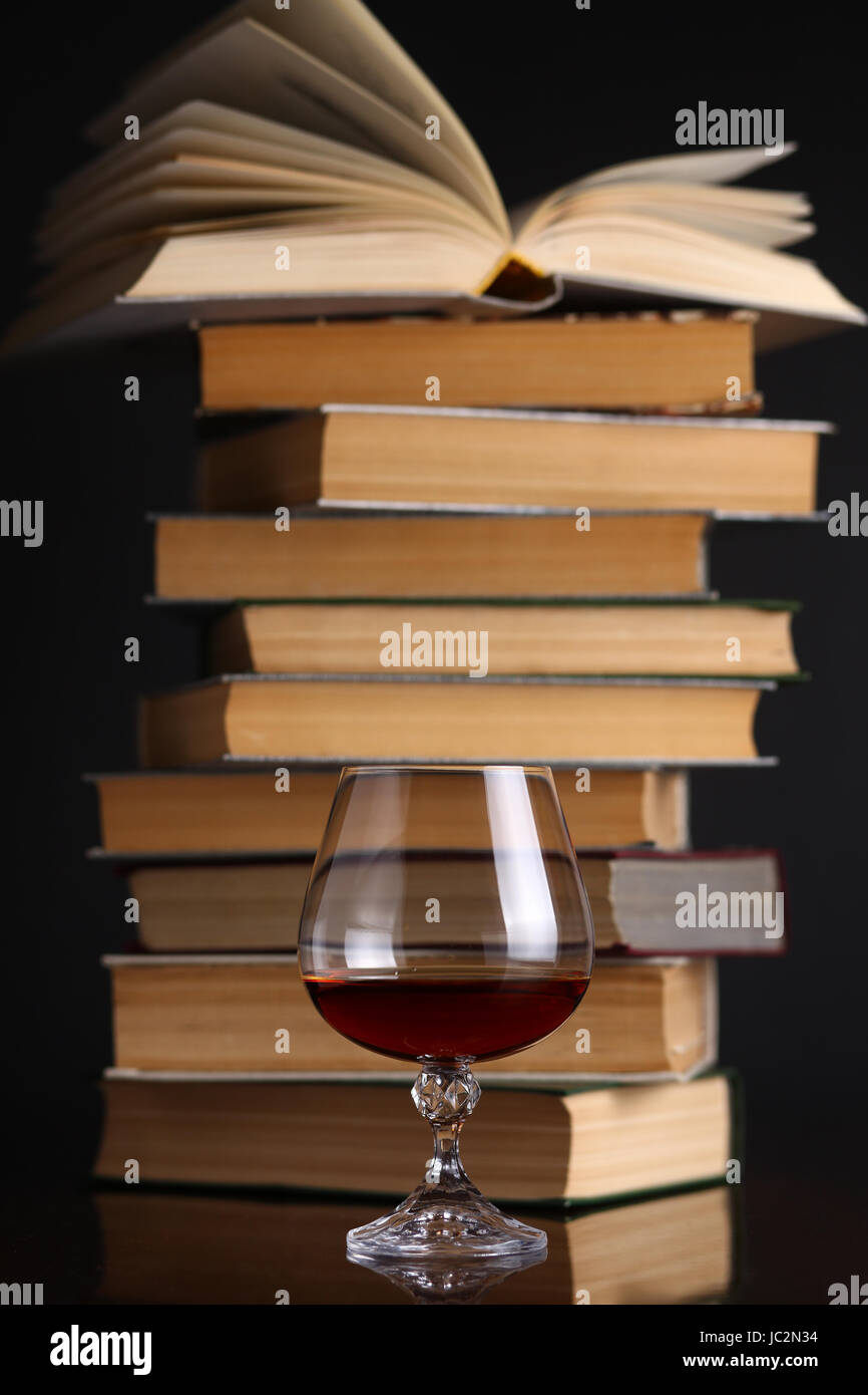 Glass of brandy on a reflective surface with books Stock Photo - Alamy