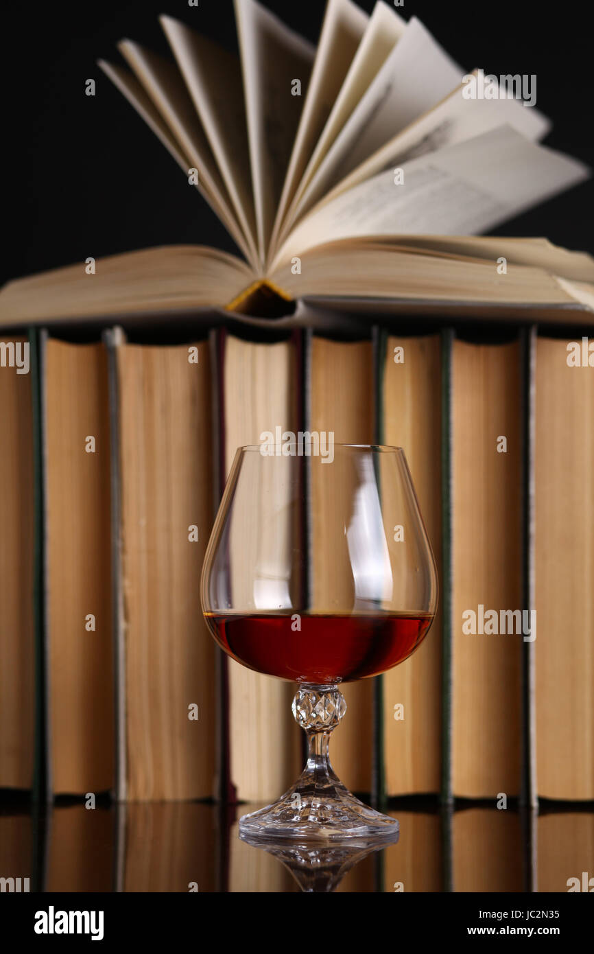 Glass of brandy on a reflective surface with books Stock Photo - Alamy