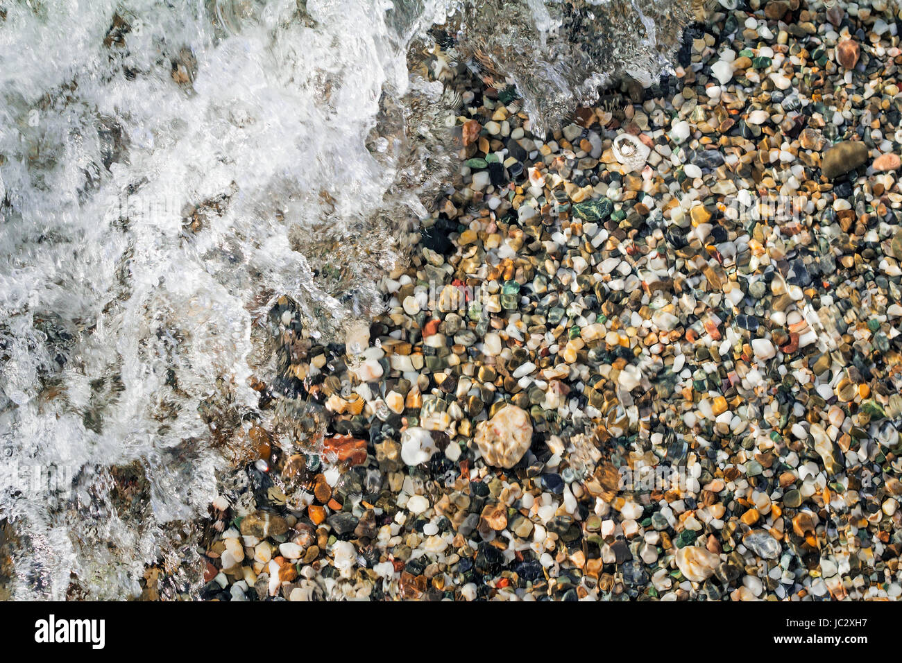 Small multi-colored sea stones on the beach, covered with transparent ...
