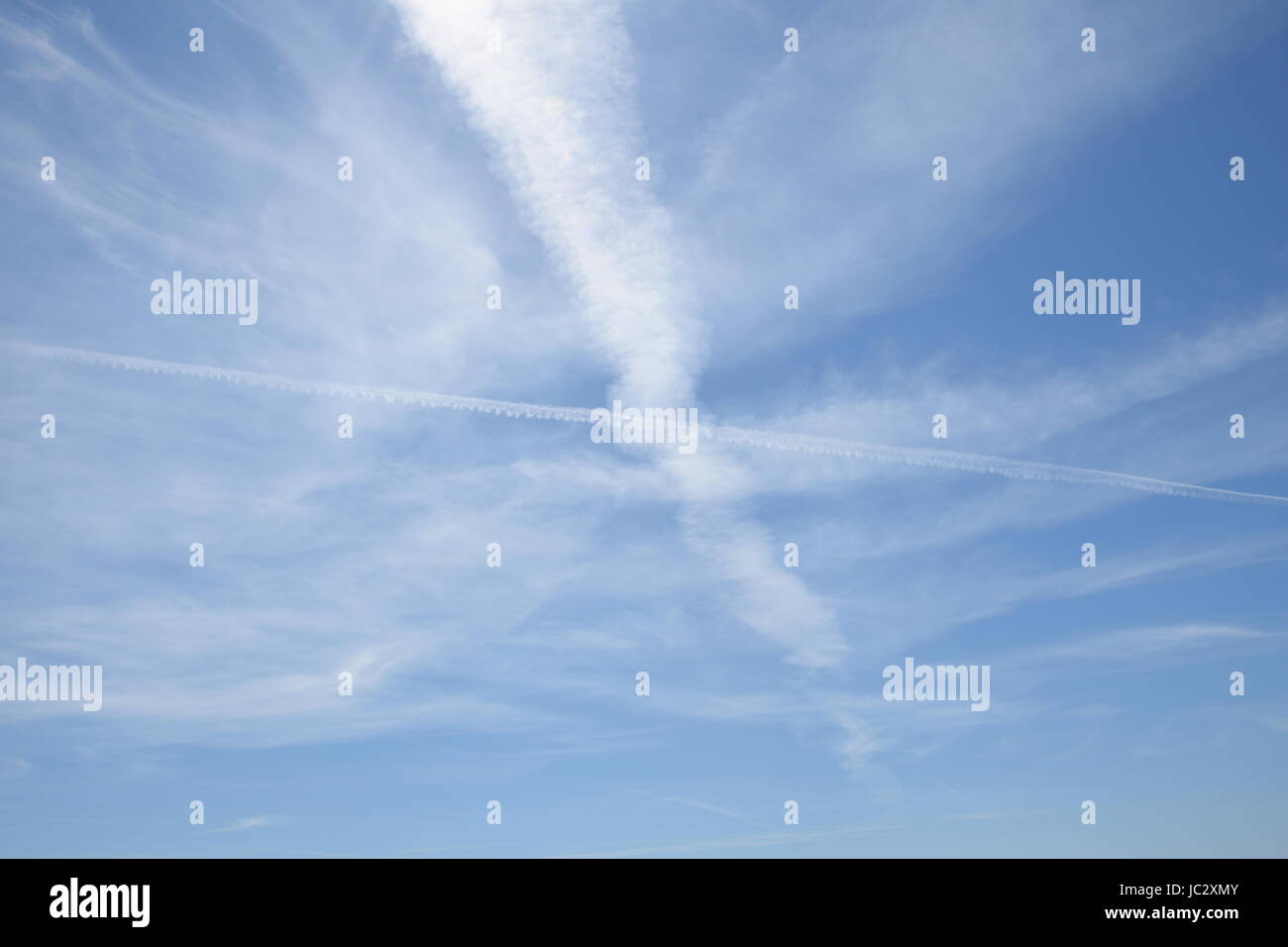 Jet trails, known as chemtrails or contrails over blue sky background ...