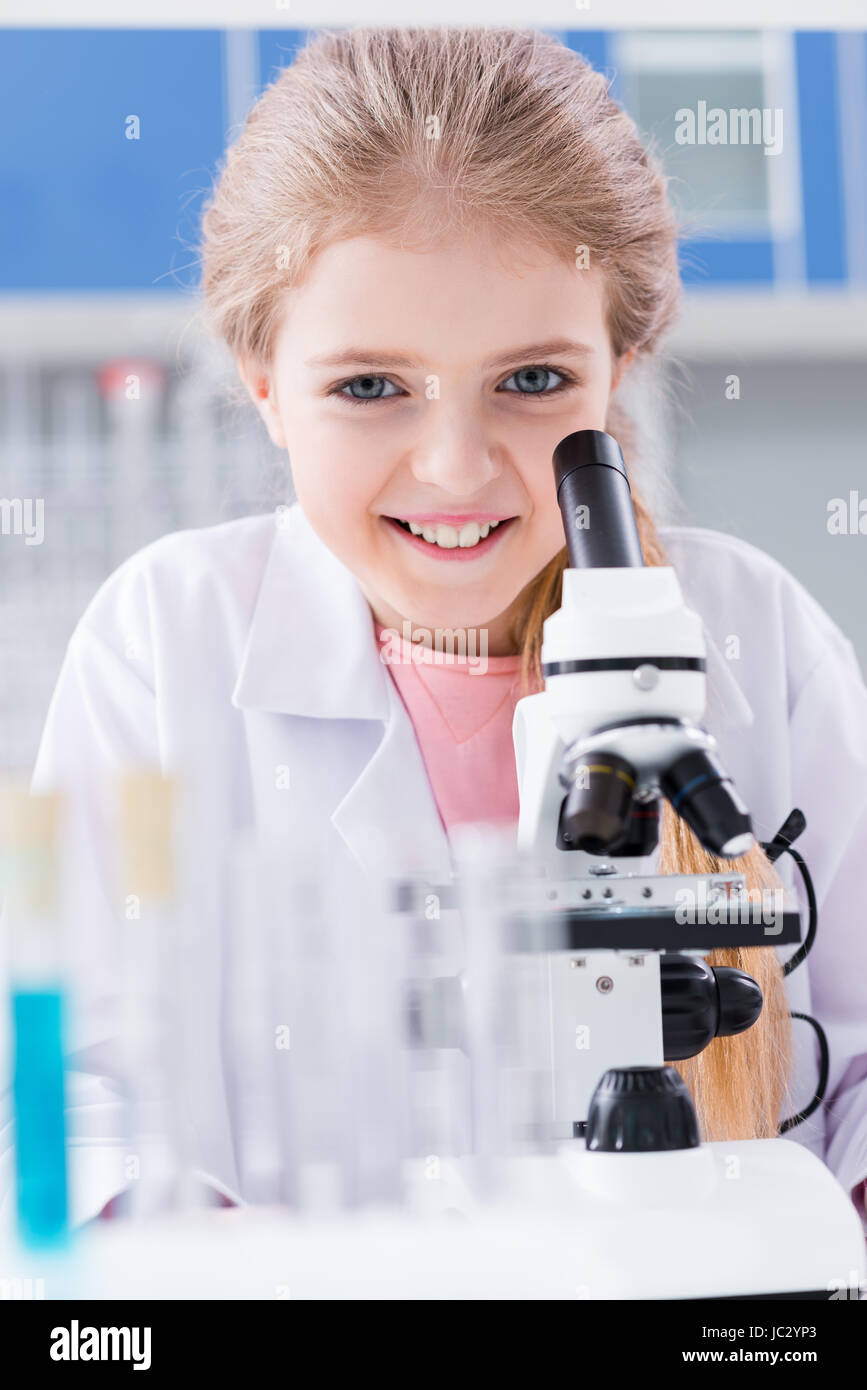 Smiling little girl in white working with microscope in chemical lab ...