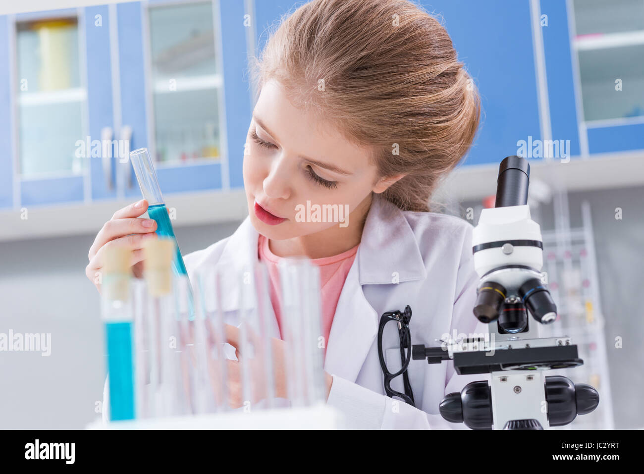 Focused little girl in white coat examining test tube with reagent in ...