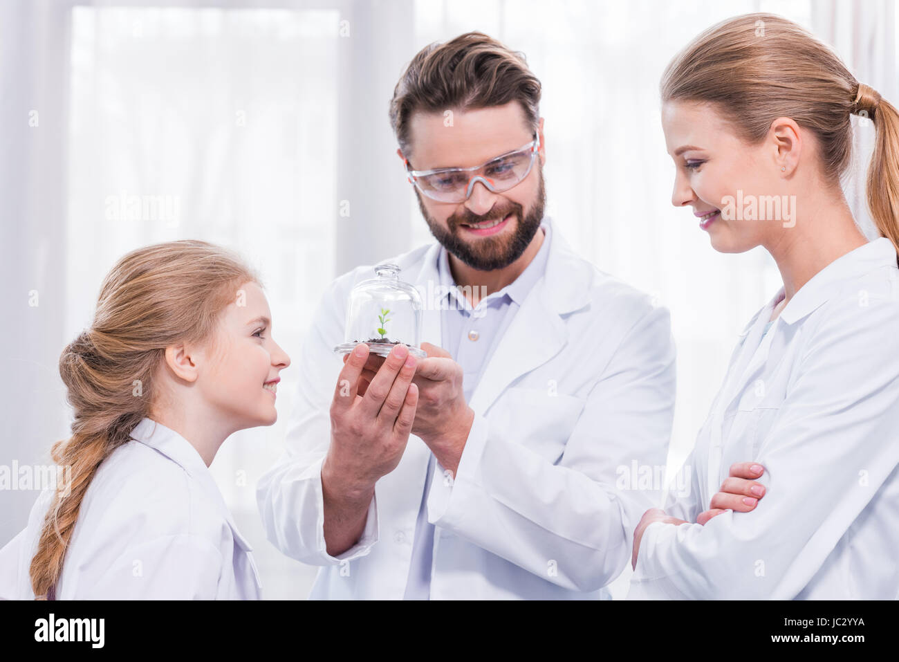 Smiling teachers scientists and student looking at green plant in ...
