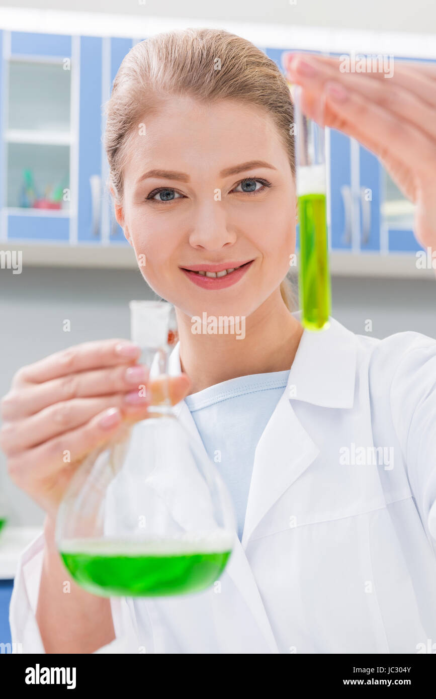 Beautiful young scientist holding flasks with reagents and smiling at ...