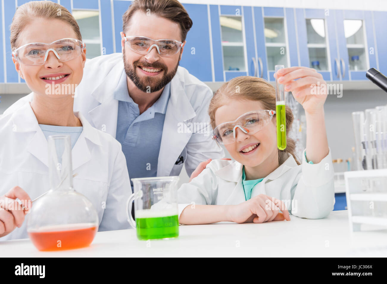 adult scientists and little girl in goggles with tubes in laboratory ...