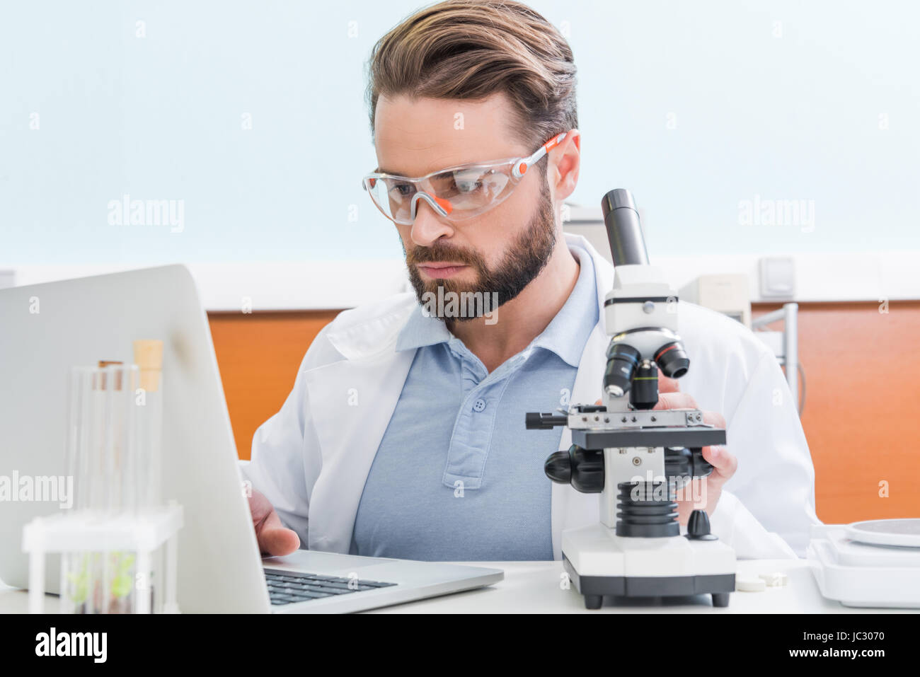 concentrated bearded scientist working with microscope and laptop in ...