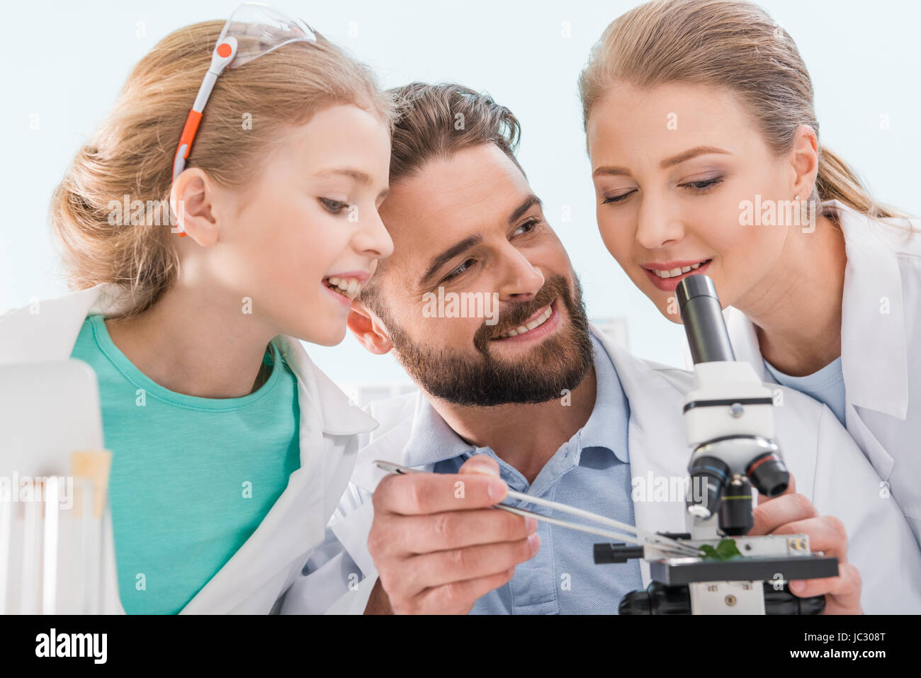 smiling adult scientists and little girl with microscope in laboratory ...