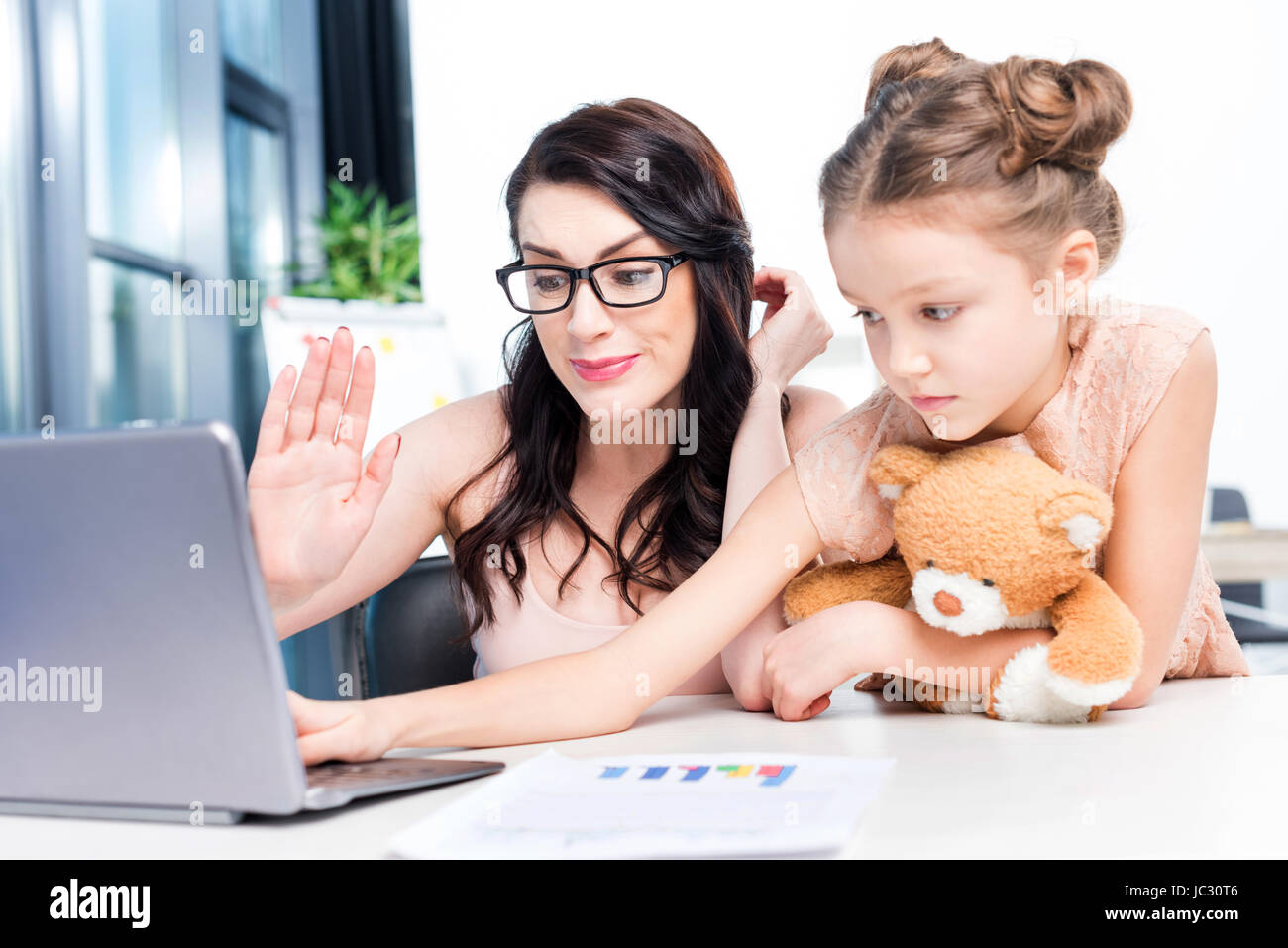 young businesswoman working with little adorable daughter in office ...
