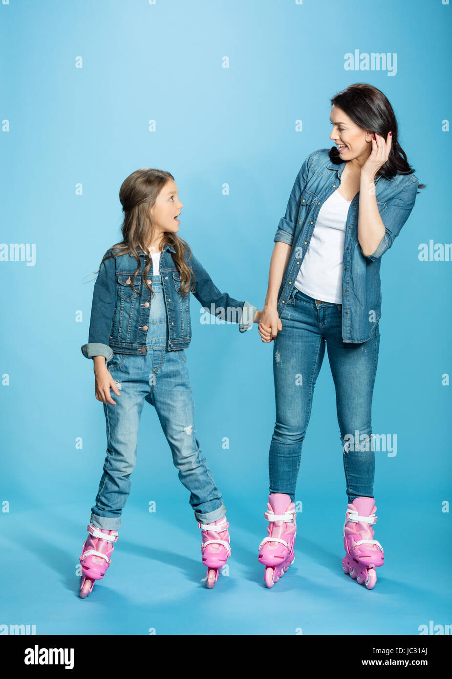 mother and daughter in roller skates holding hands in studio on blue ...