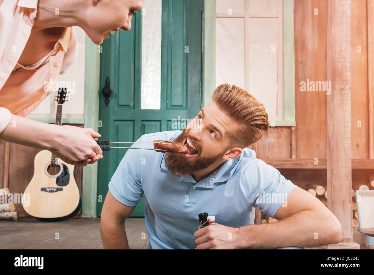 couple roasting meat and vegetables on barbecue grill, man biting piece ...