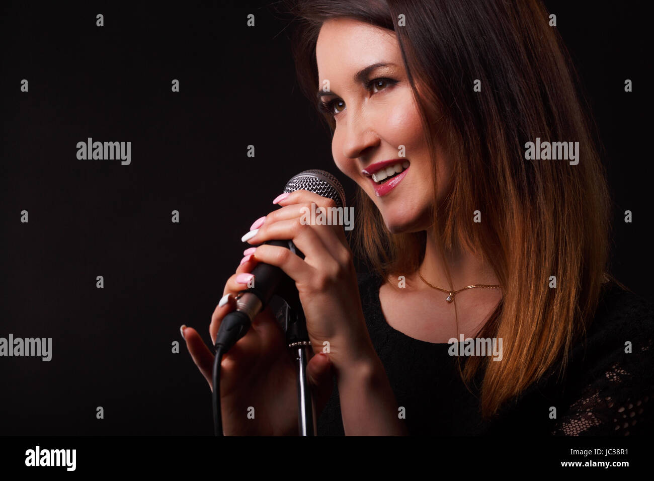 Portrait of girl with microphone in hands isolated on black background ...