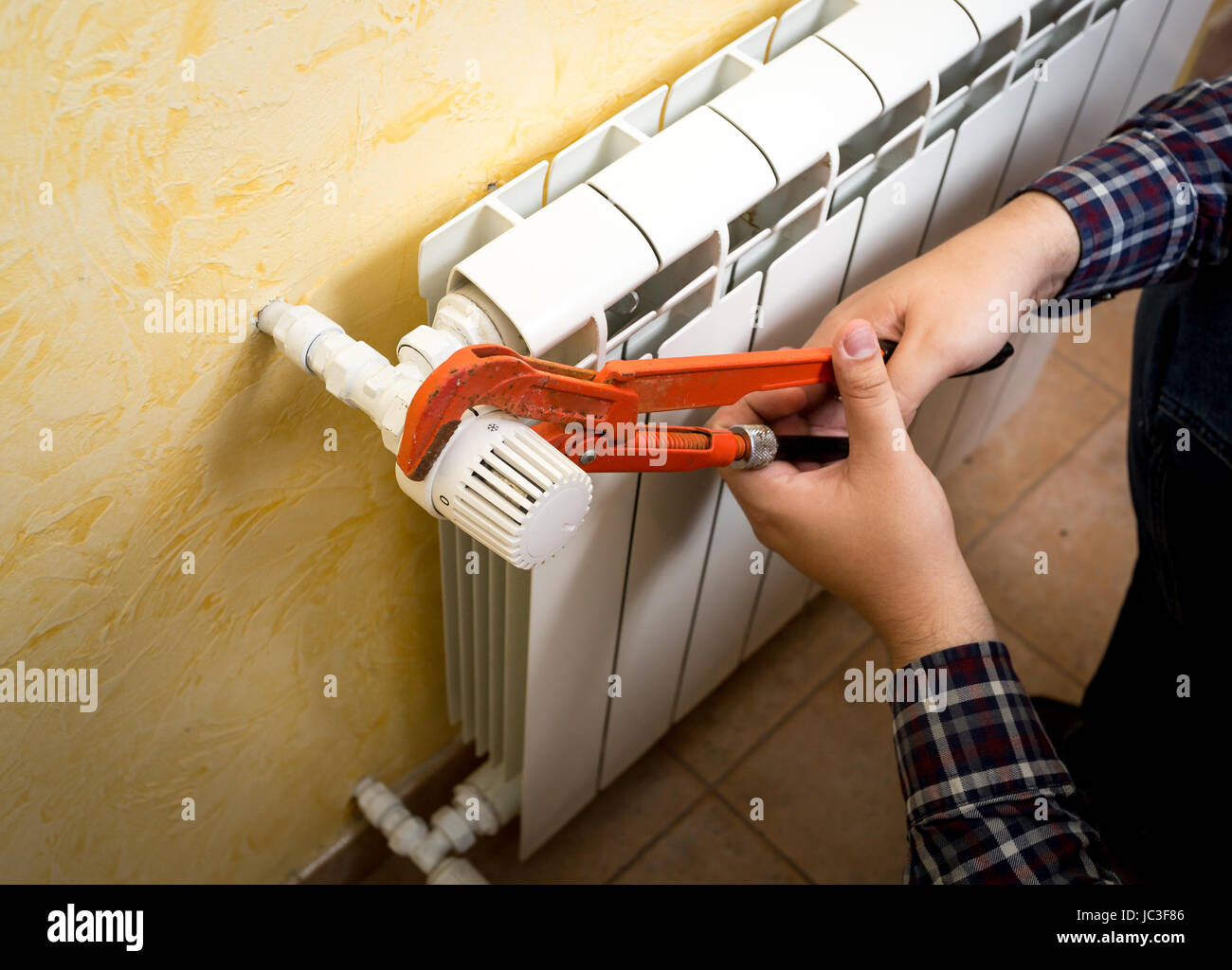 Closeup shot of man installing radiator valve with red plumber pliers ...