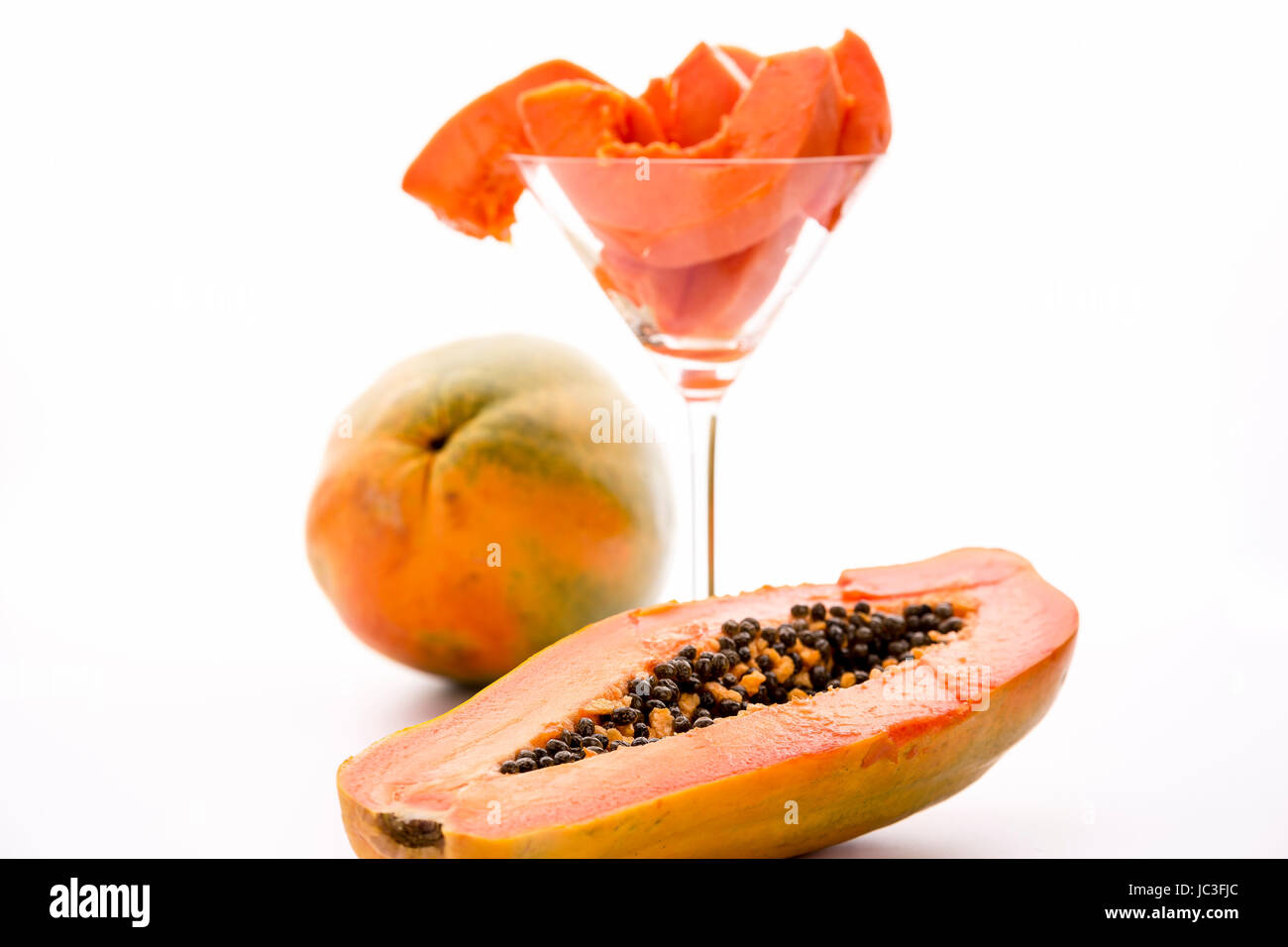 The central cavity of a halved papaya in focus and behind it a glass ...