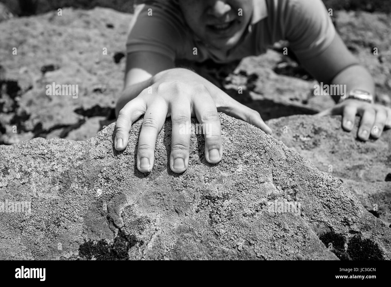 Black and white closeup photo of man holding on cliff on one hand Stock ...