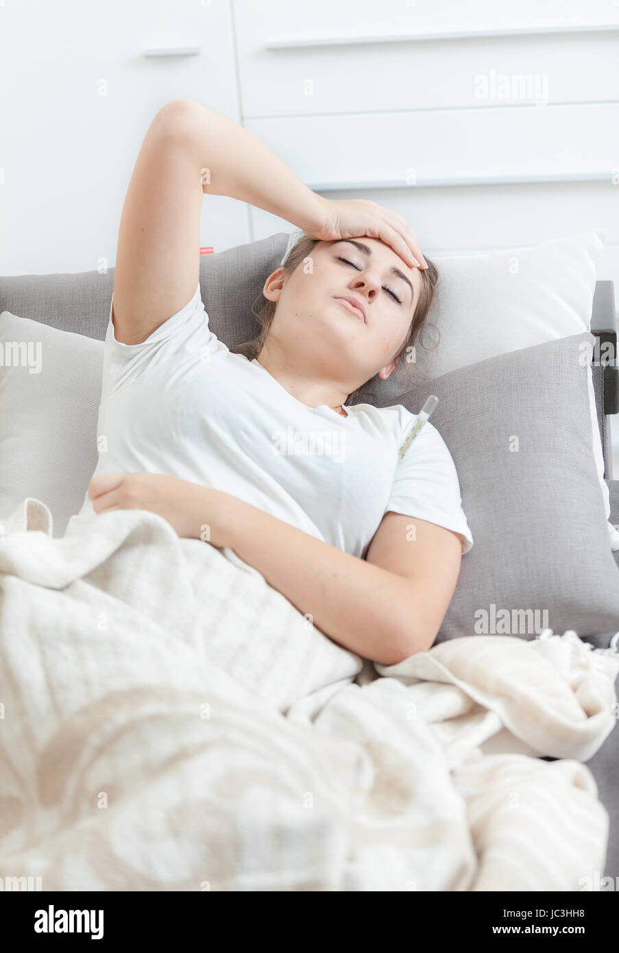 Portrait of sick woman taking temperature while lying on bed Stock ...