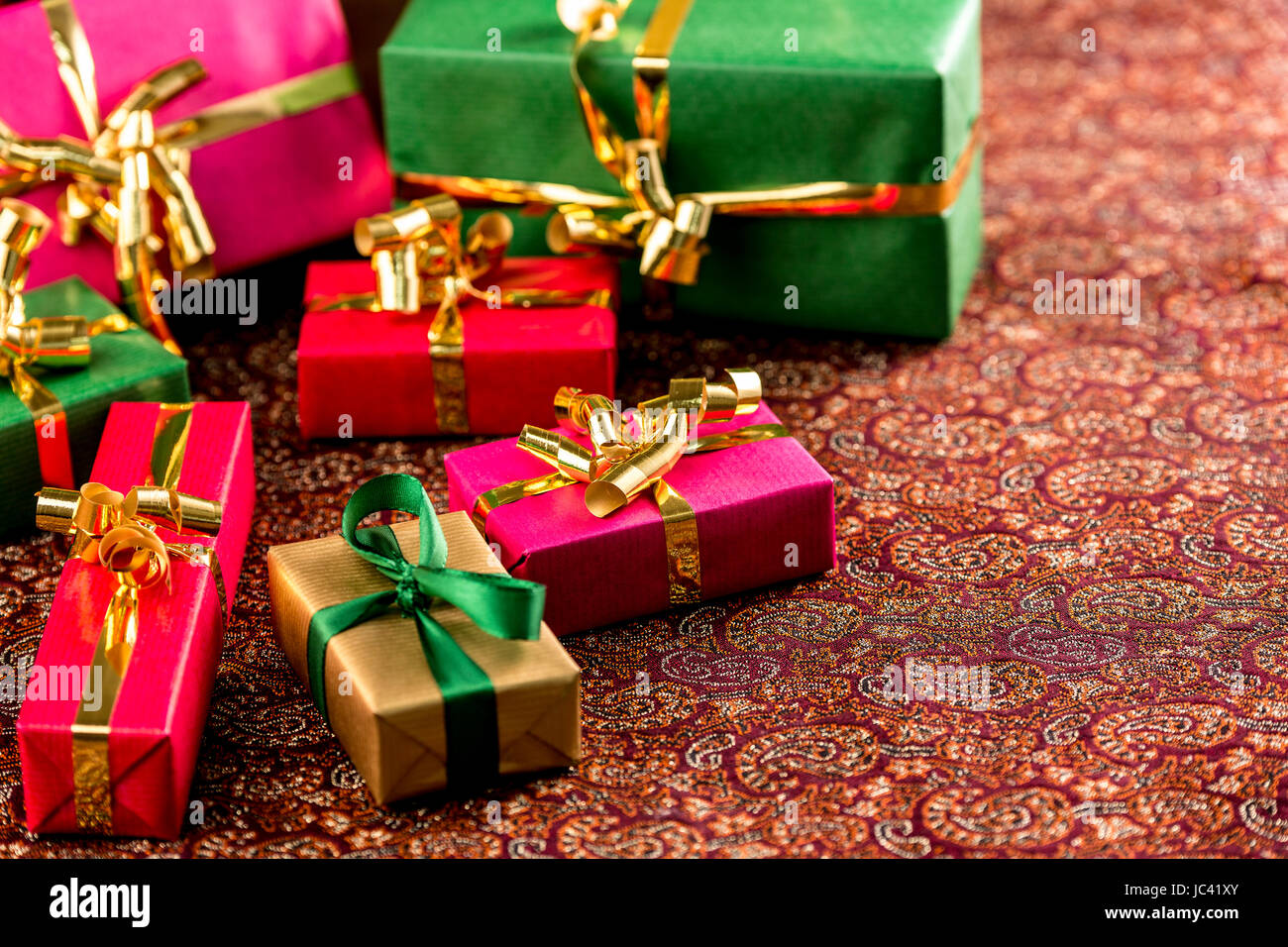 Seven presents wrapped in green, magenta, red and gold. All with bows ...