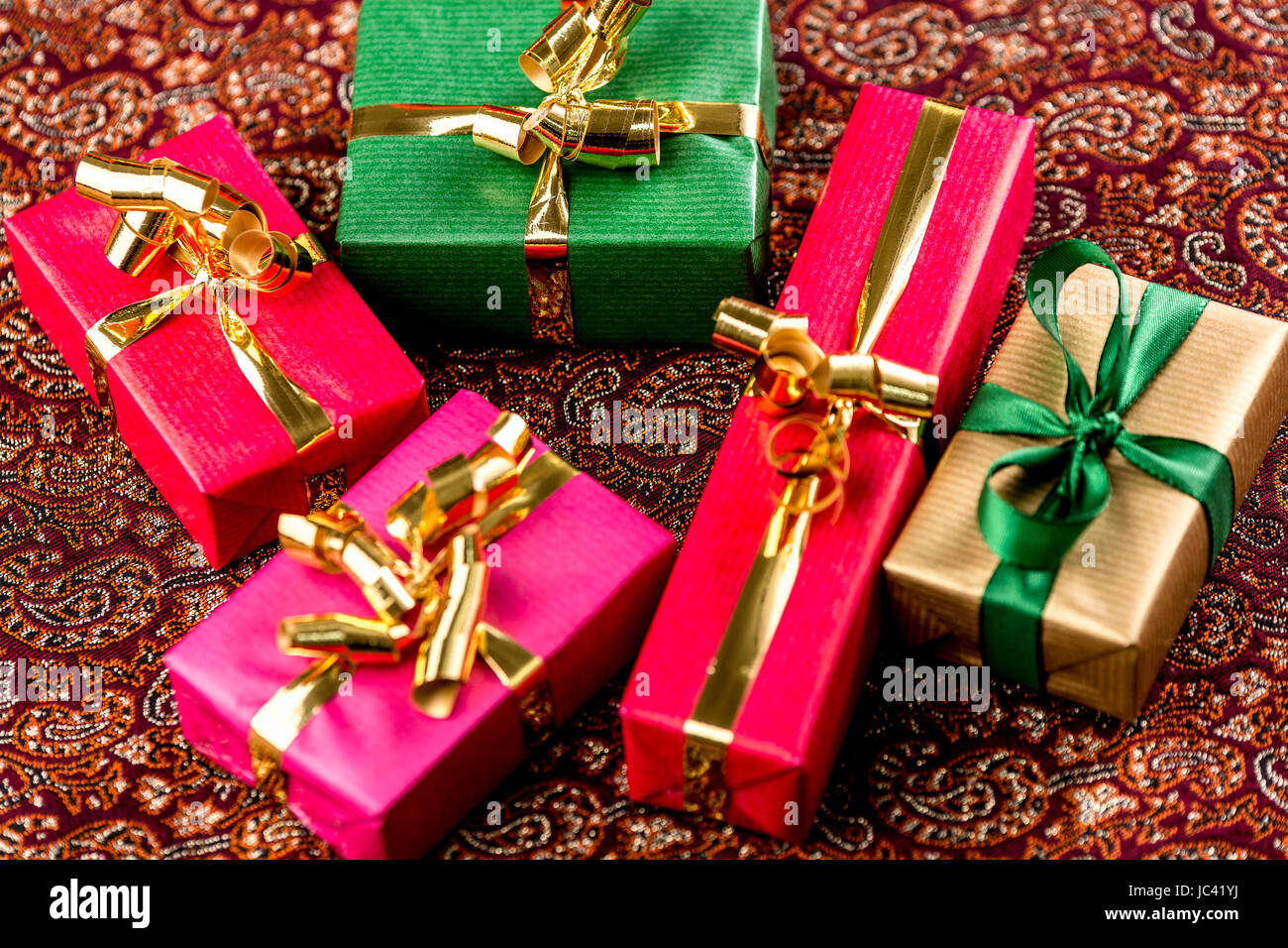 Five plain presents placed on a festive cloth. Bows in gold and green ...