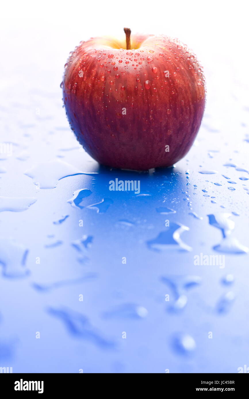 Whole red apple on wet blue surface Stock Photo - Alamy