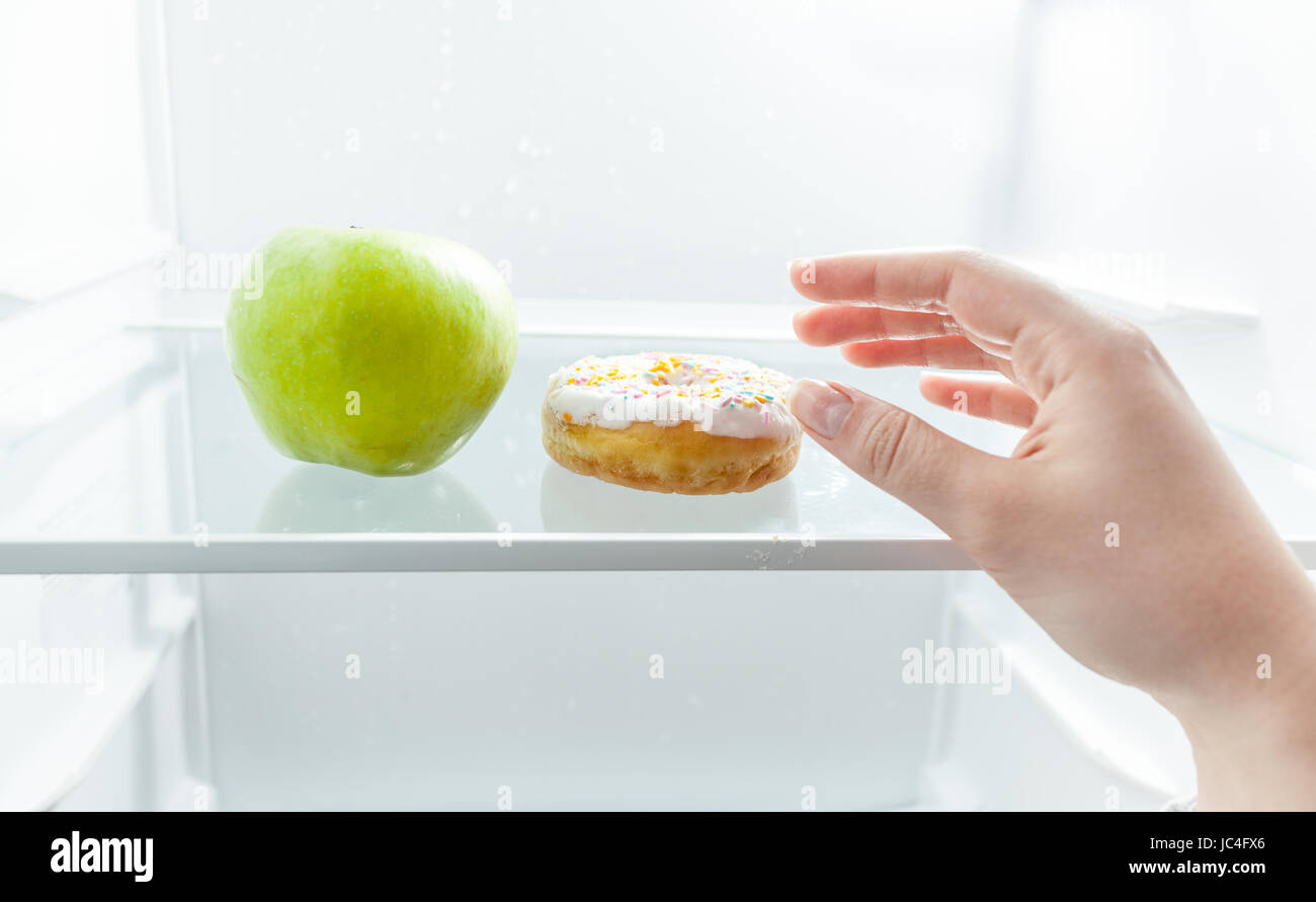 Closeup portrait of hand choosing between apple and donut at fridge ...