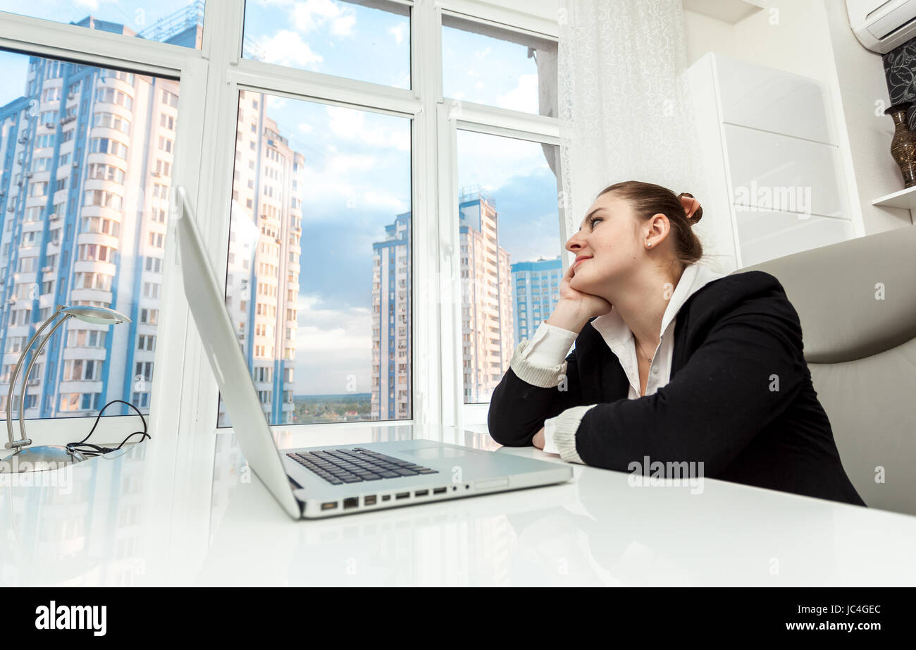 Portrait of young businesswoman sitting behind table and looking out of ...