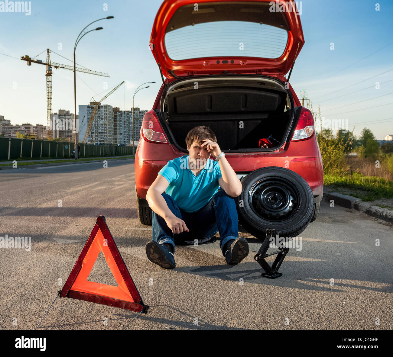 Sad and depressed man sitting near car with punctured tire Stock Photo ...