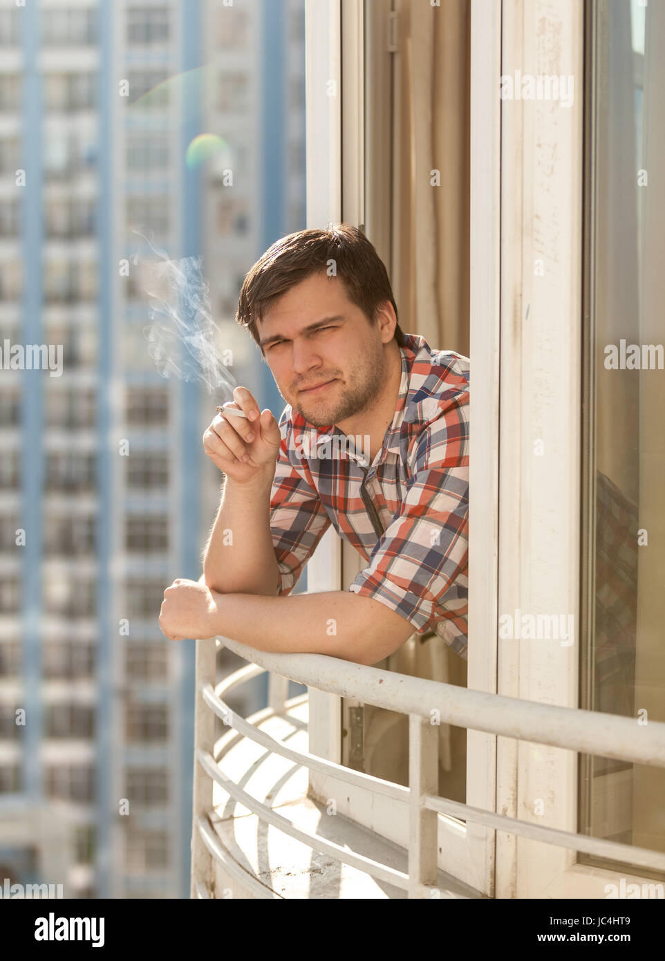 Handsome young man smoking cigarette on balcony Stock Photo - Alamy