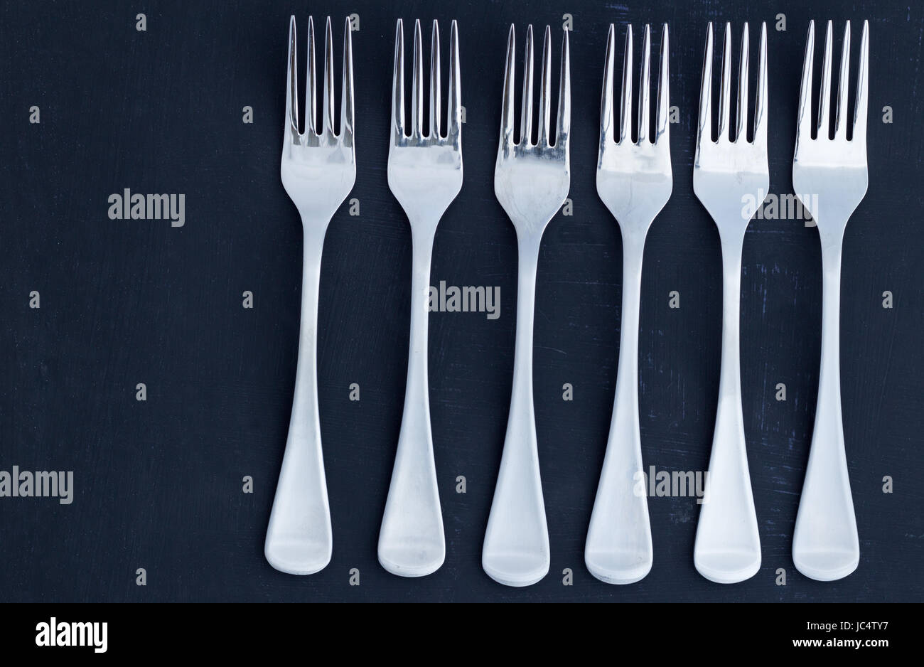Five steel dinner forks in a row on black board background Stock Photo ...
