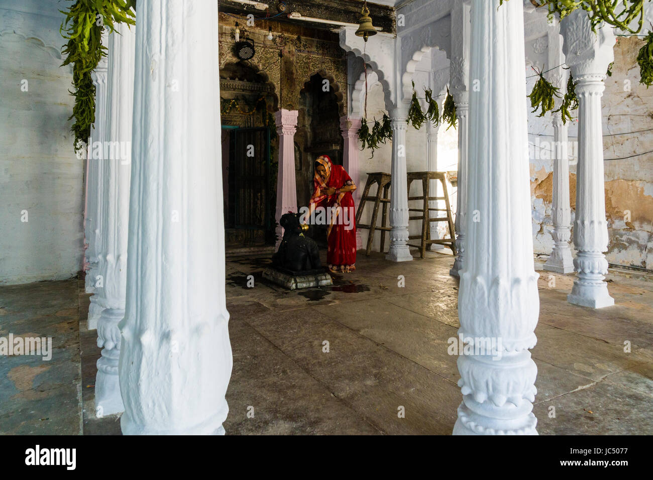 A woman is doing Pooja, offerings to the Gods, in a small hindu temple ...