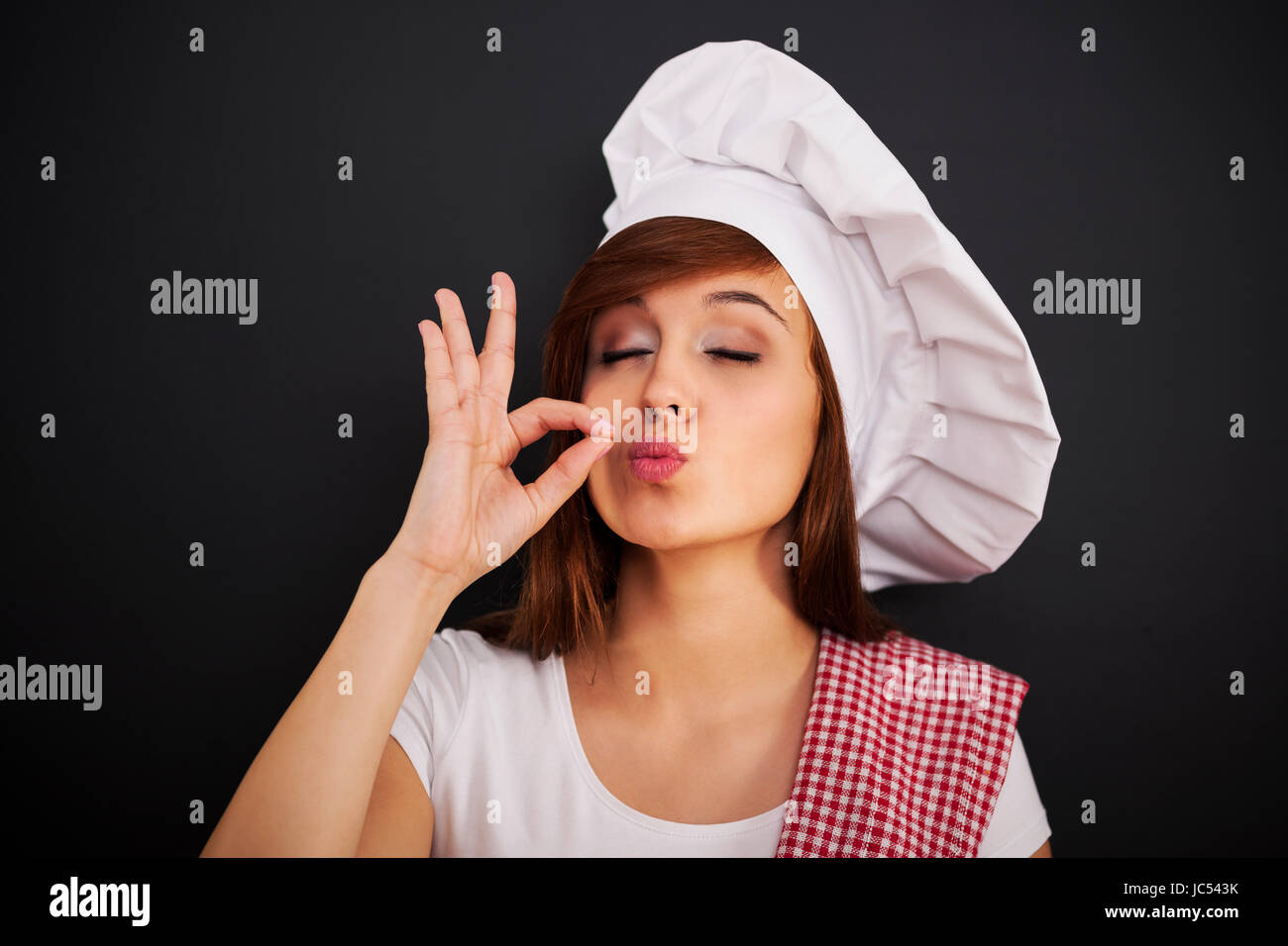 Beautiful young female chef with hand sign Stock Photo - Alamy