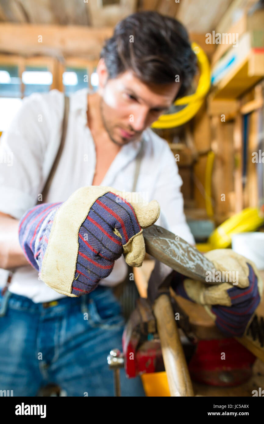 Young man in the Bavarian mountains grinds his axe and sharpening tools ...