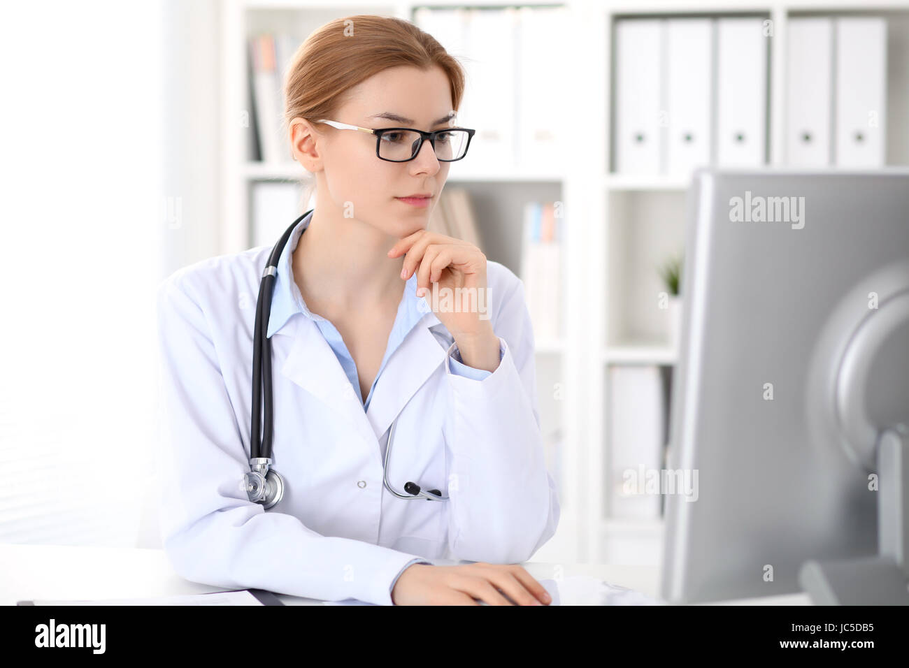 Young brunette female doctor sitting at the table and working by ...